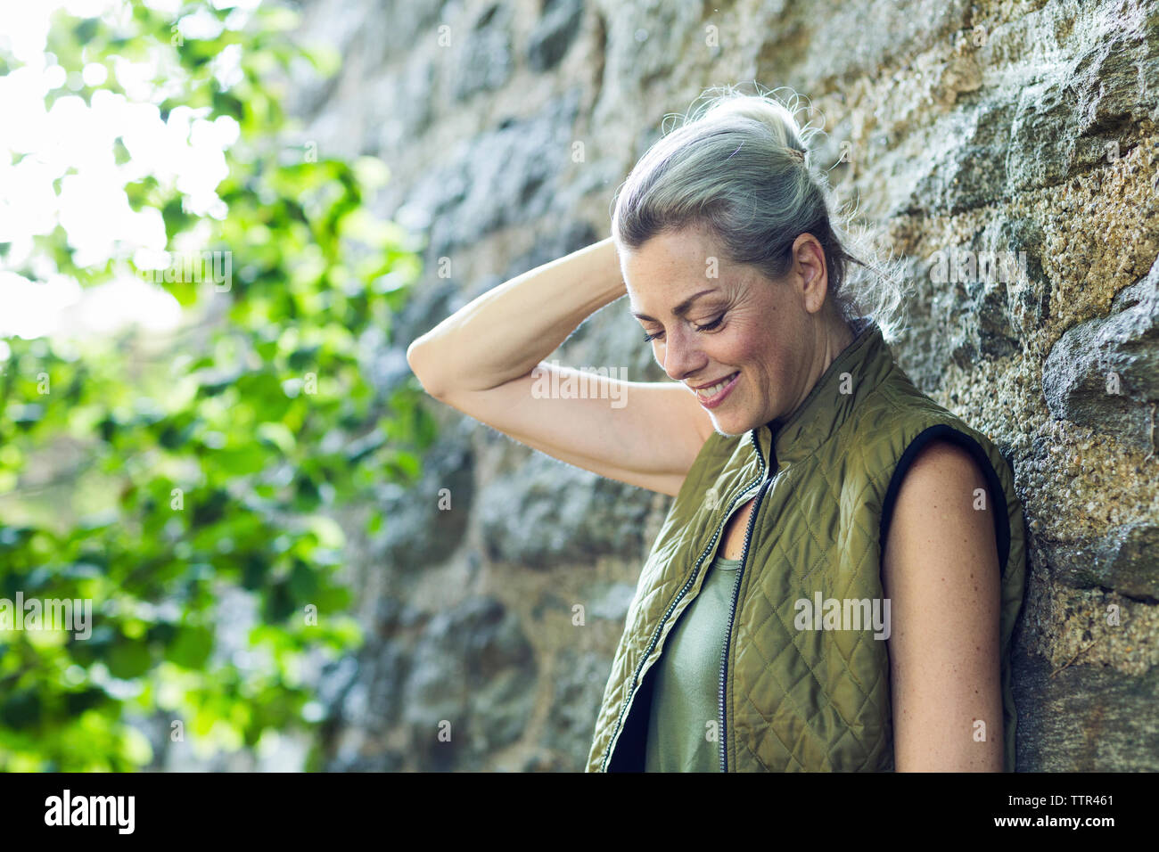 Happy woman standing against stone wall Stock Photo - Alamy
