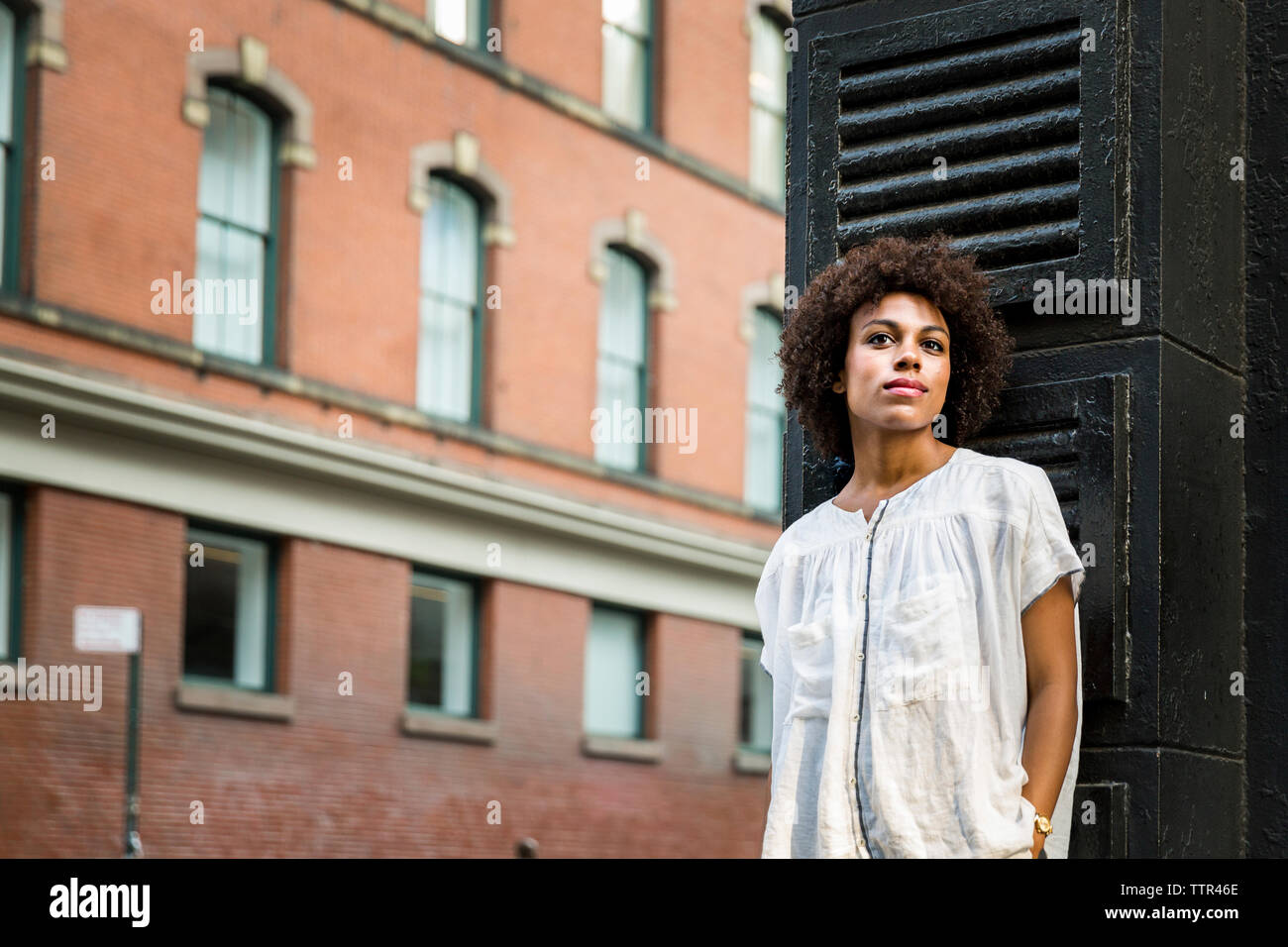 Low angle view of thoughtful woman looking away against building in ...