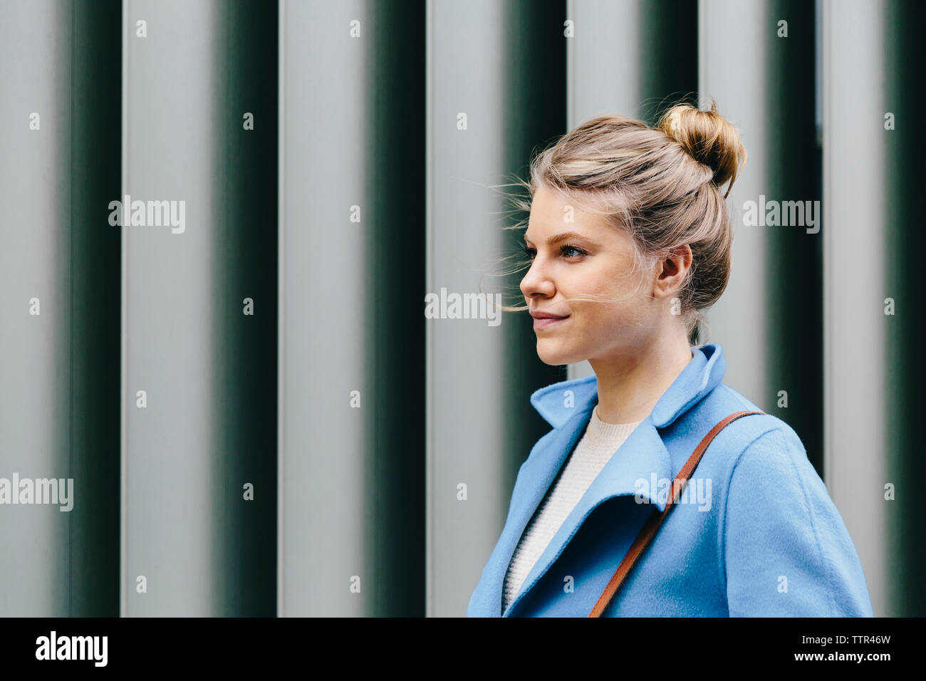 Side view of confident young woman wearing trench coat against shutter ...