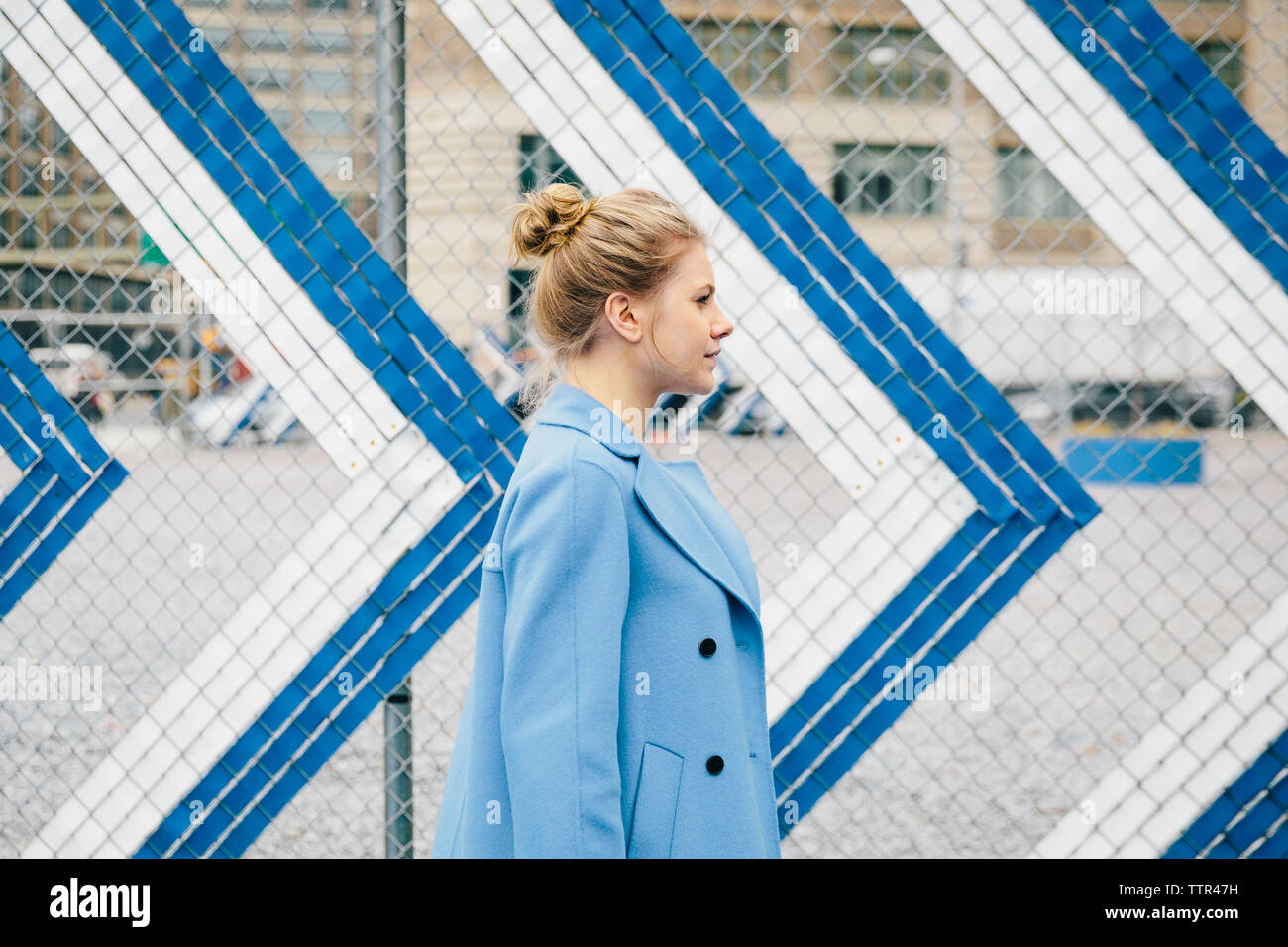 Side view of young woman wearing trench coat while walking against ...