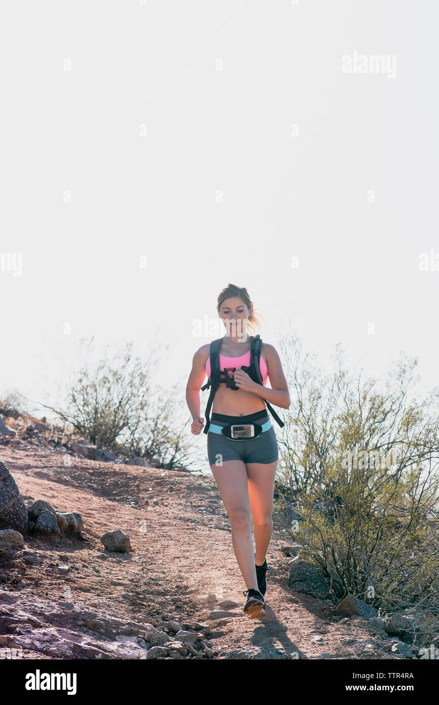Female hiker running on mountain against clear sky during sunny day ...
