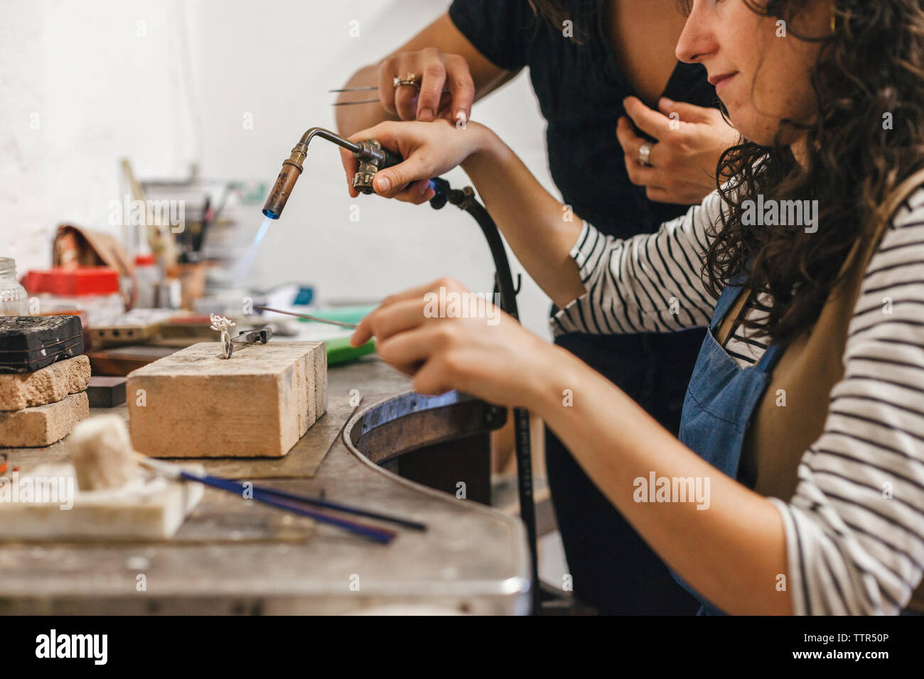 Midsection of female teacher assisting student in using blow torch on ...