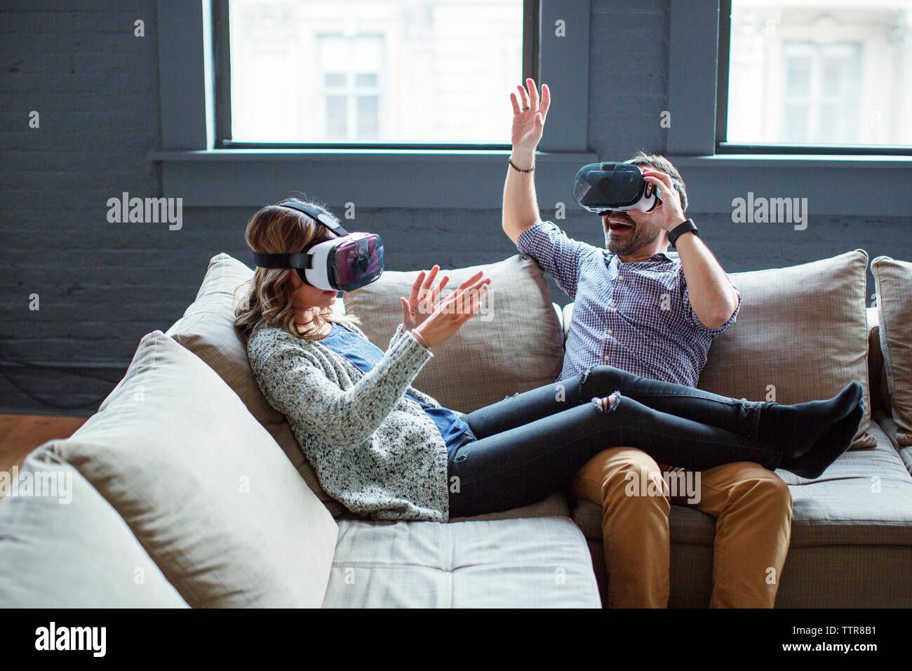 Colleagues wearing virtual reality simulators while sitting on sofa in ...