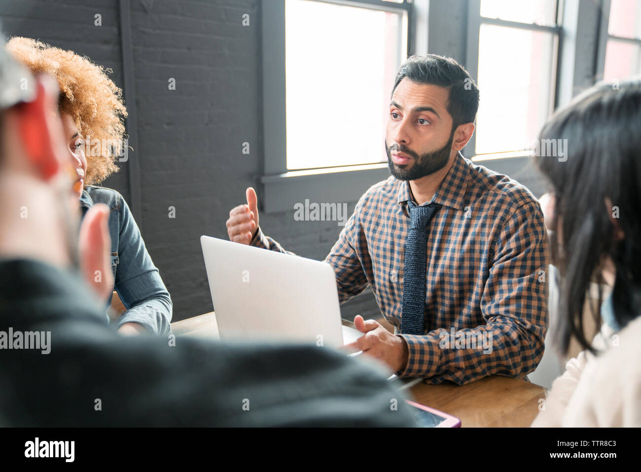 Man explaining to coworkers at table in office Stock Photo - Alamy
