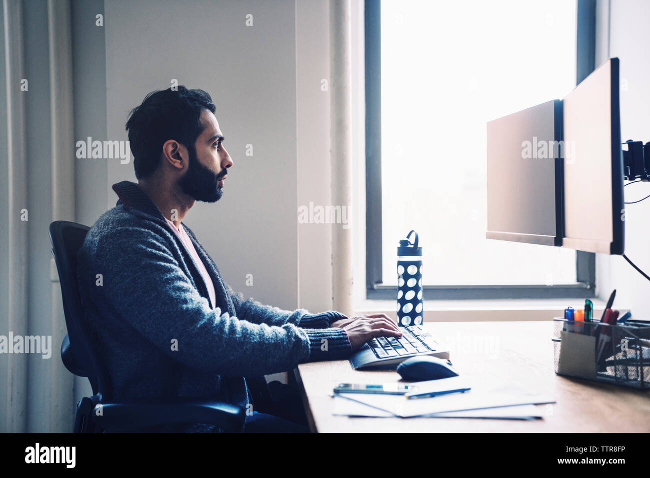 Side view of businessman using desktop computer while sitting at desk ...