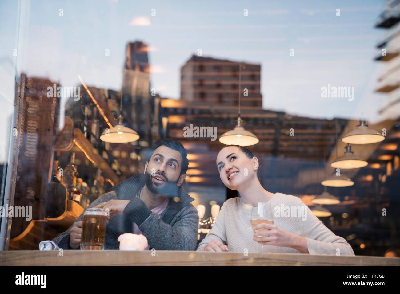 Couple enjoying drinks while looking away seen through restaurant ...