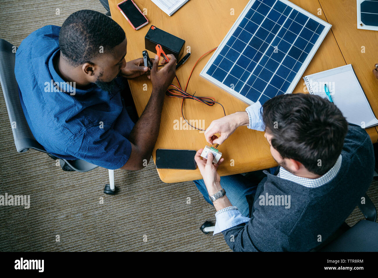 Overhead view of businessmen working on solar panel model in office ...