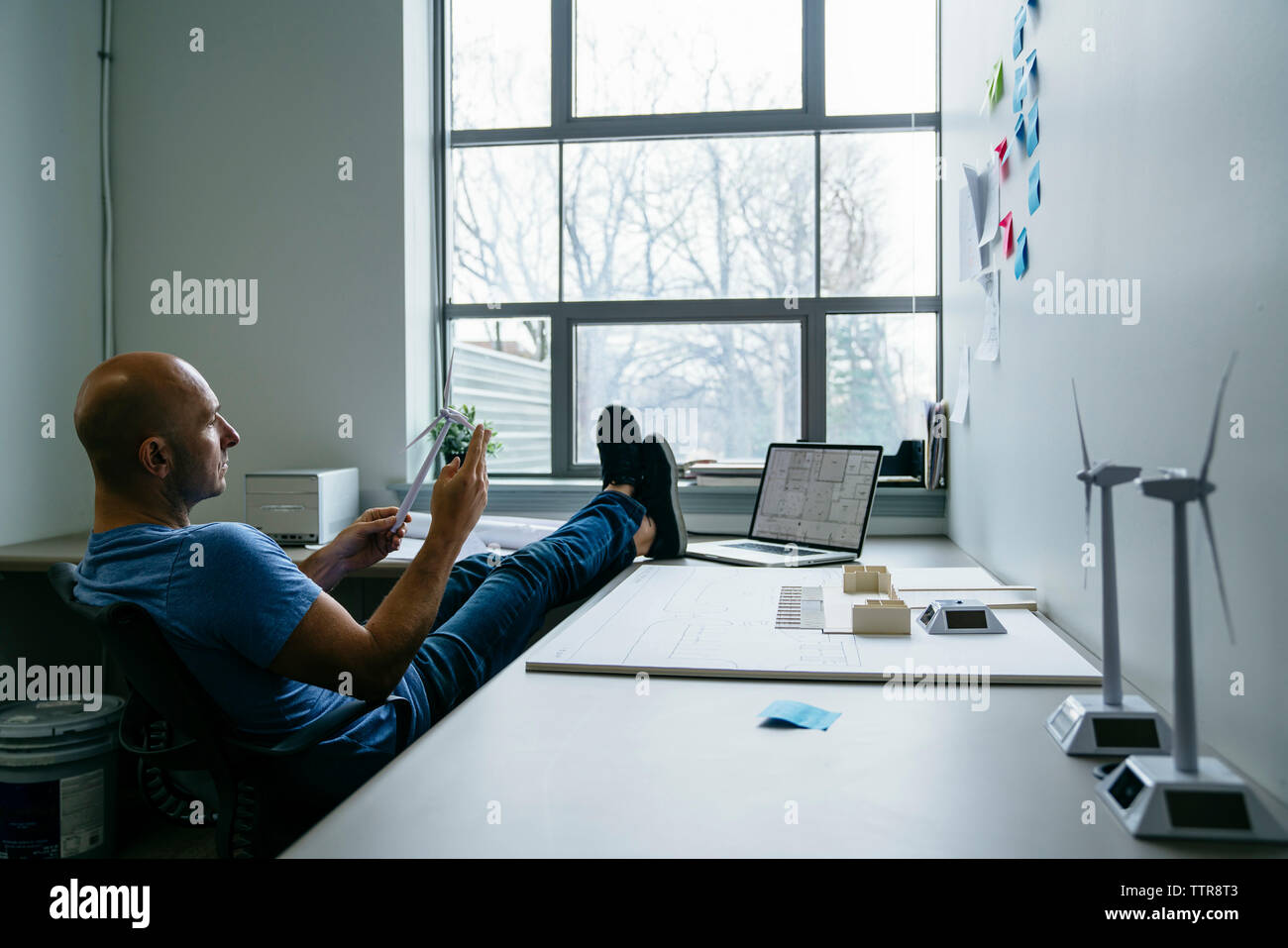 Side view of businessman holding wind turbine model while sitting with ...