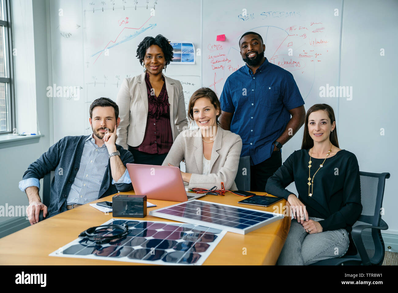 Portrait of smiling business people by solar panel models on desk Stock ...