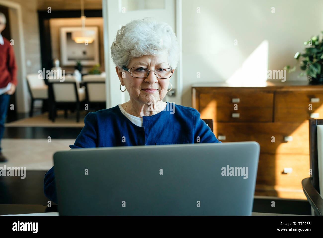 Senior woman using laptop computer at home with senior man in ...