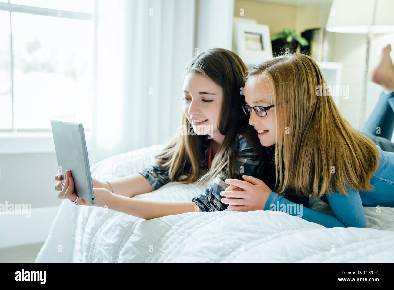 Sisters using tablet computer while lying on bed Stock Photo - Alamy