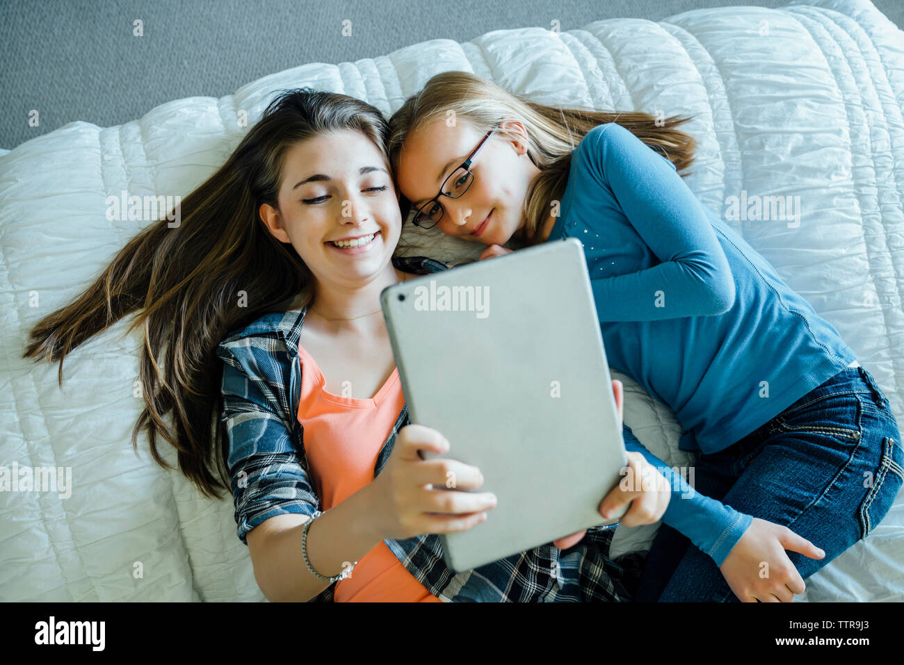 High angle view of happy sisters using tablet computer while lying on ...