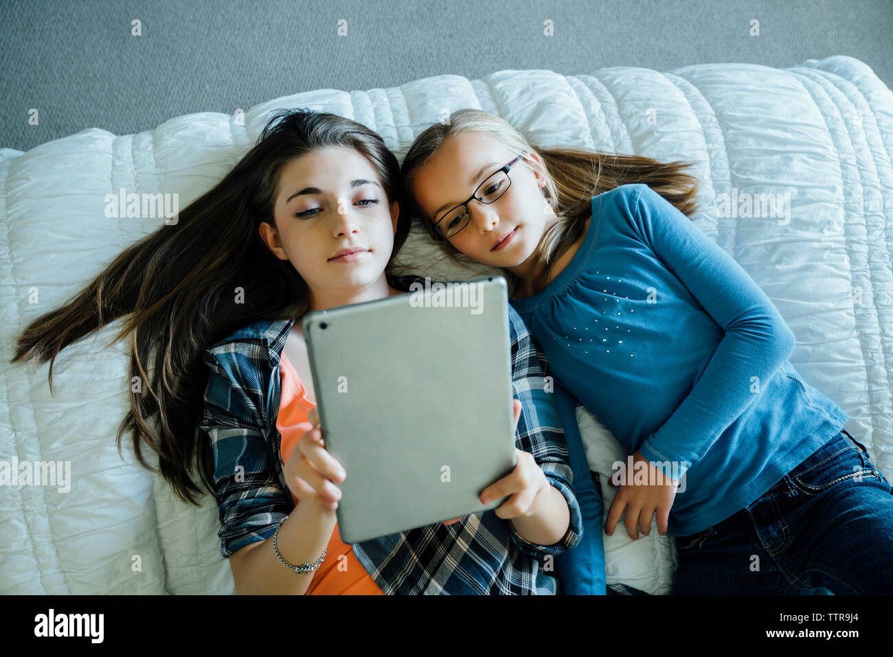 High angle view of sisters using tablet computer while lying on bed at ...