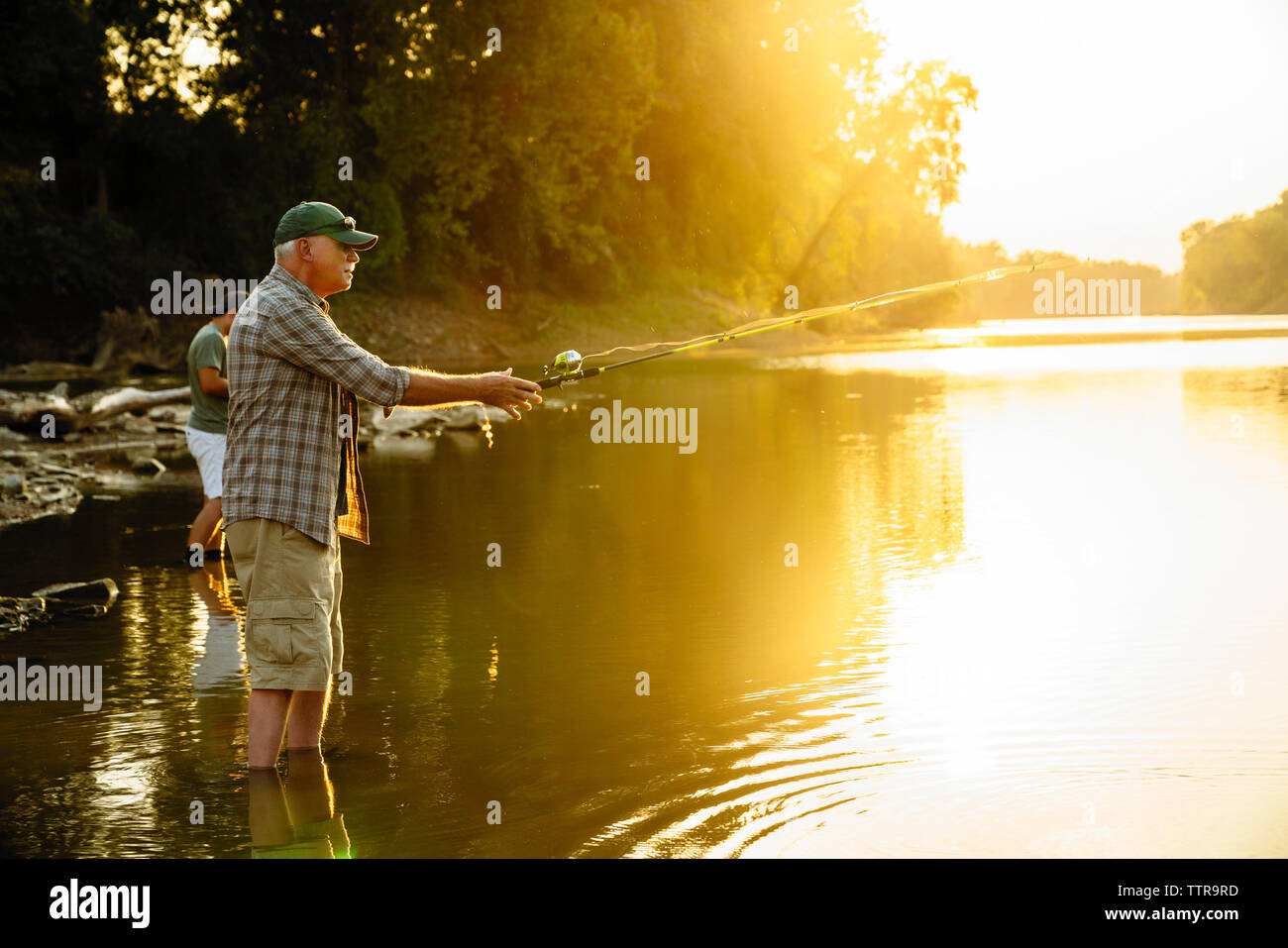 Side view of friends fishing while standing in lake during sunset Stock ...