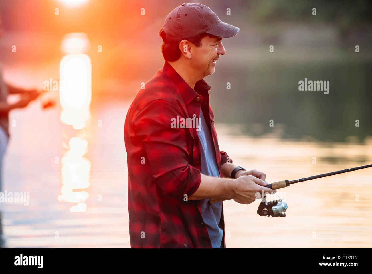 Side view of smiling man fishing in lake during sunset Stock Photo - Alamy