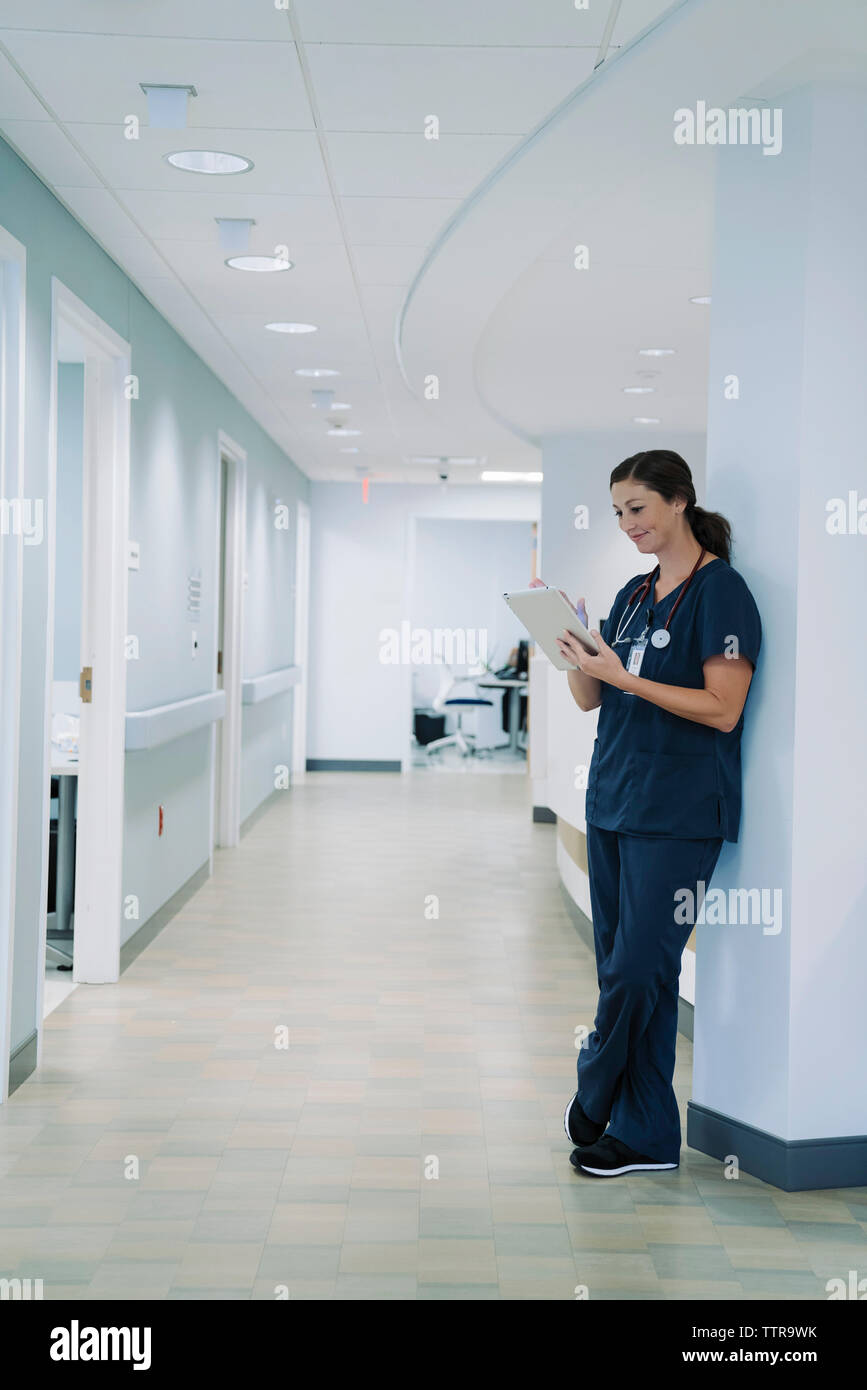 Full length of female doctor using tablet computer while leaning ...