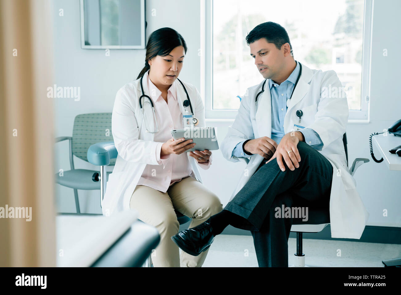Doctors discussing over tablet computer while sitting in examination ...