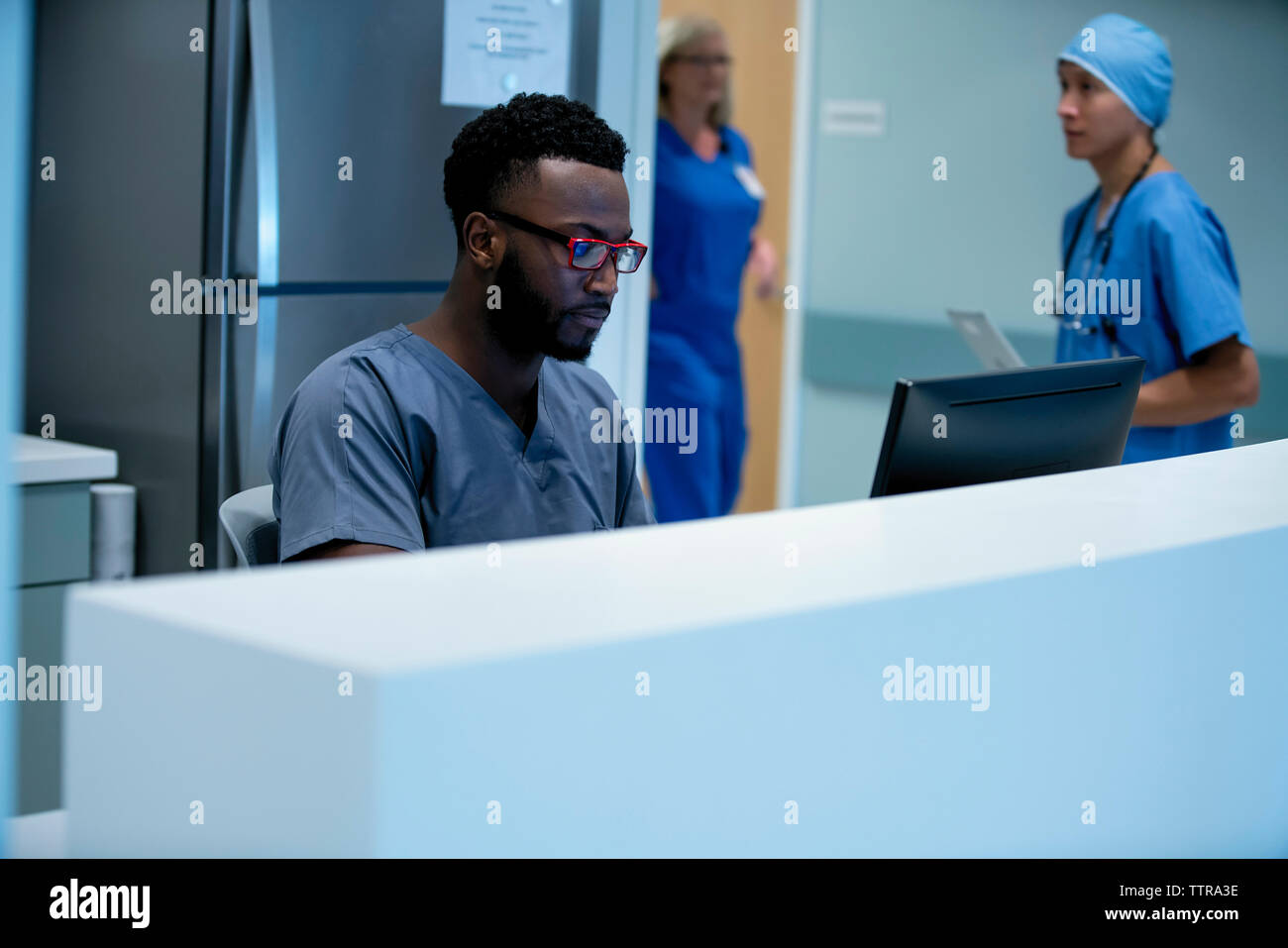 Confident doctor using desktop computer at hospital reception with ...
