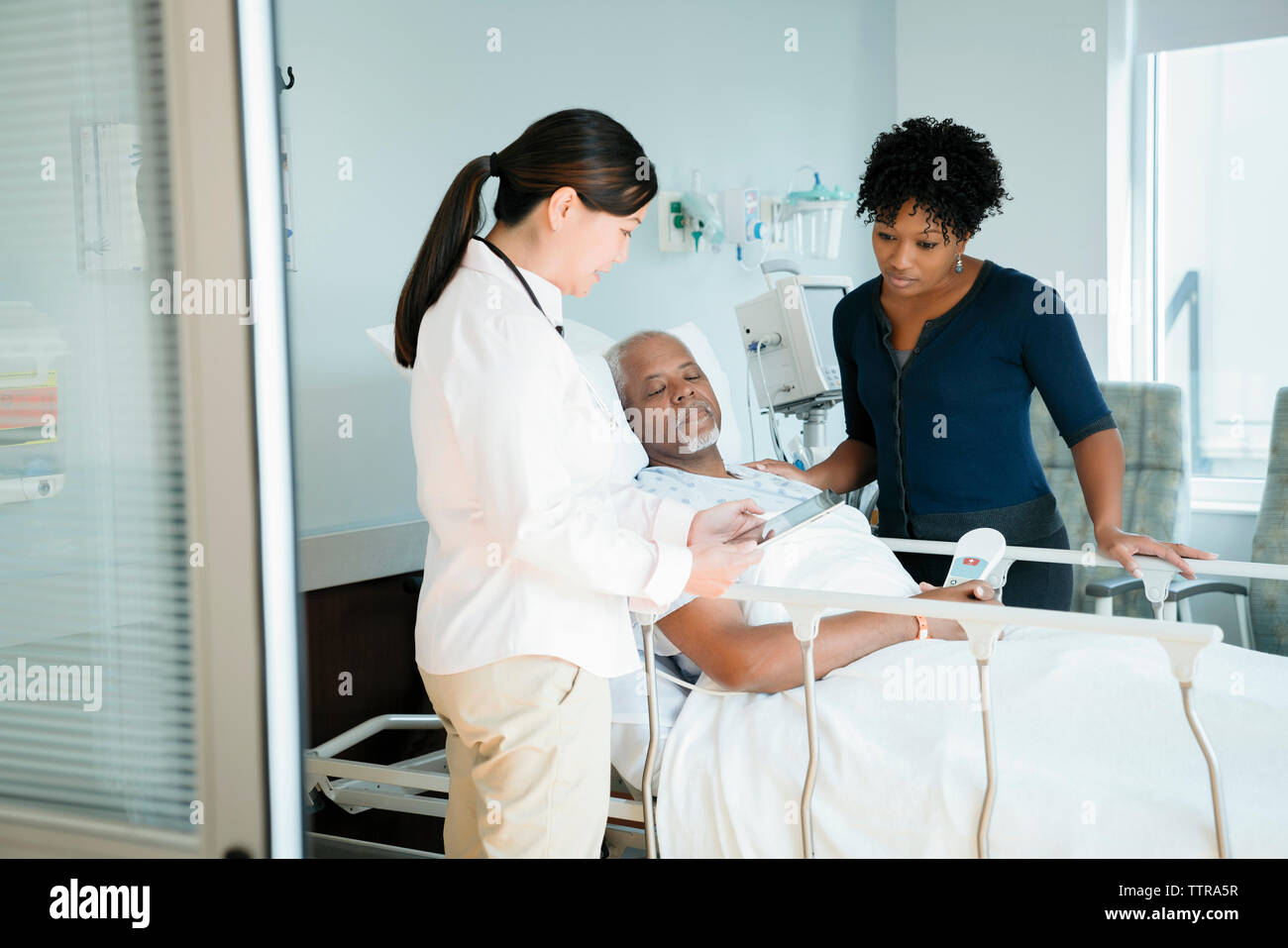 Female doctor showing tablet computer to senior patient and woman in ...