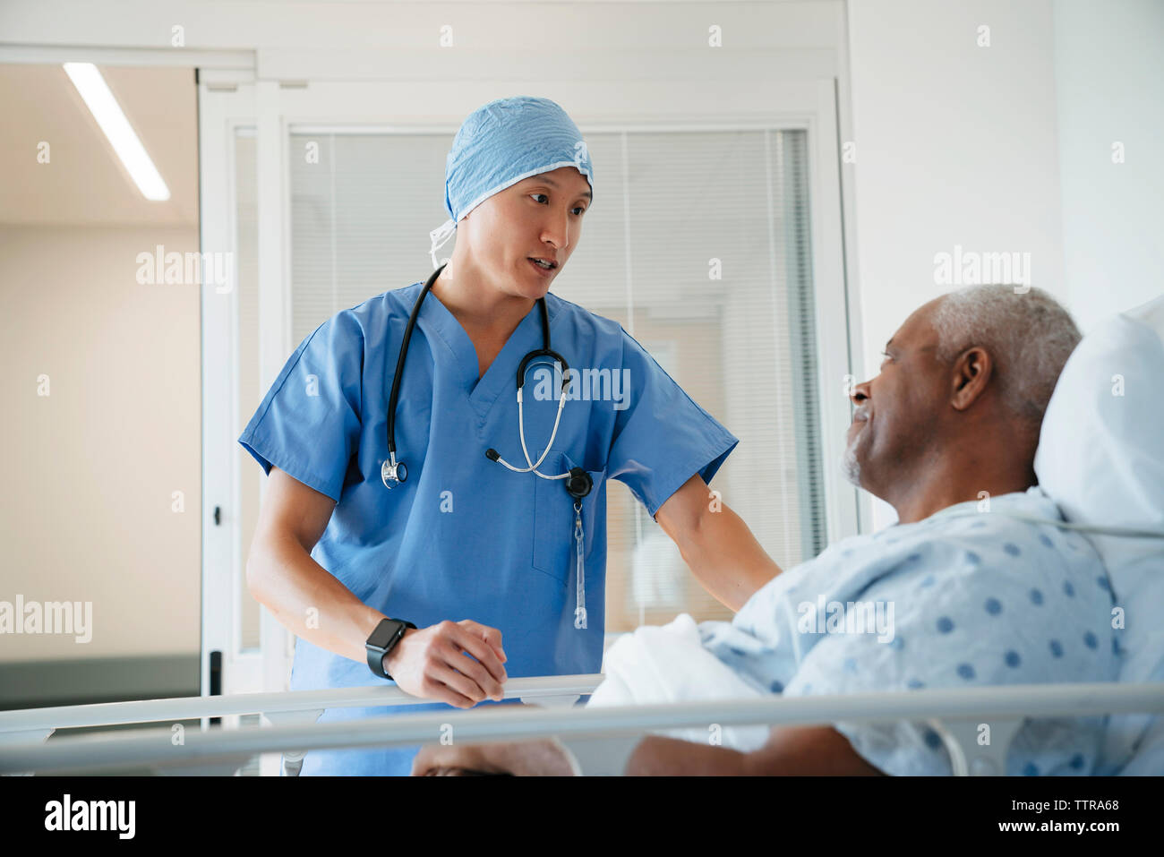 Serious surgeon talking with senior patient lying on bed in hospital ...