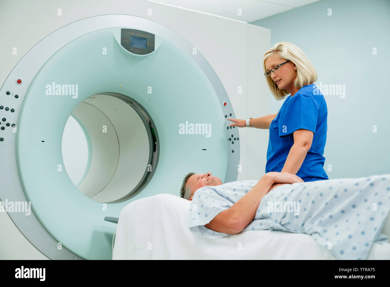 Nurse looking at patient lying on MRI Scanner while pressing start ...