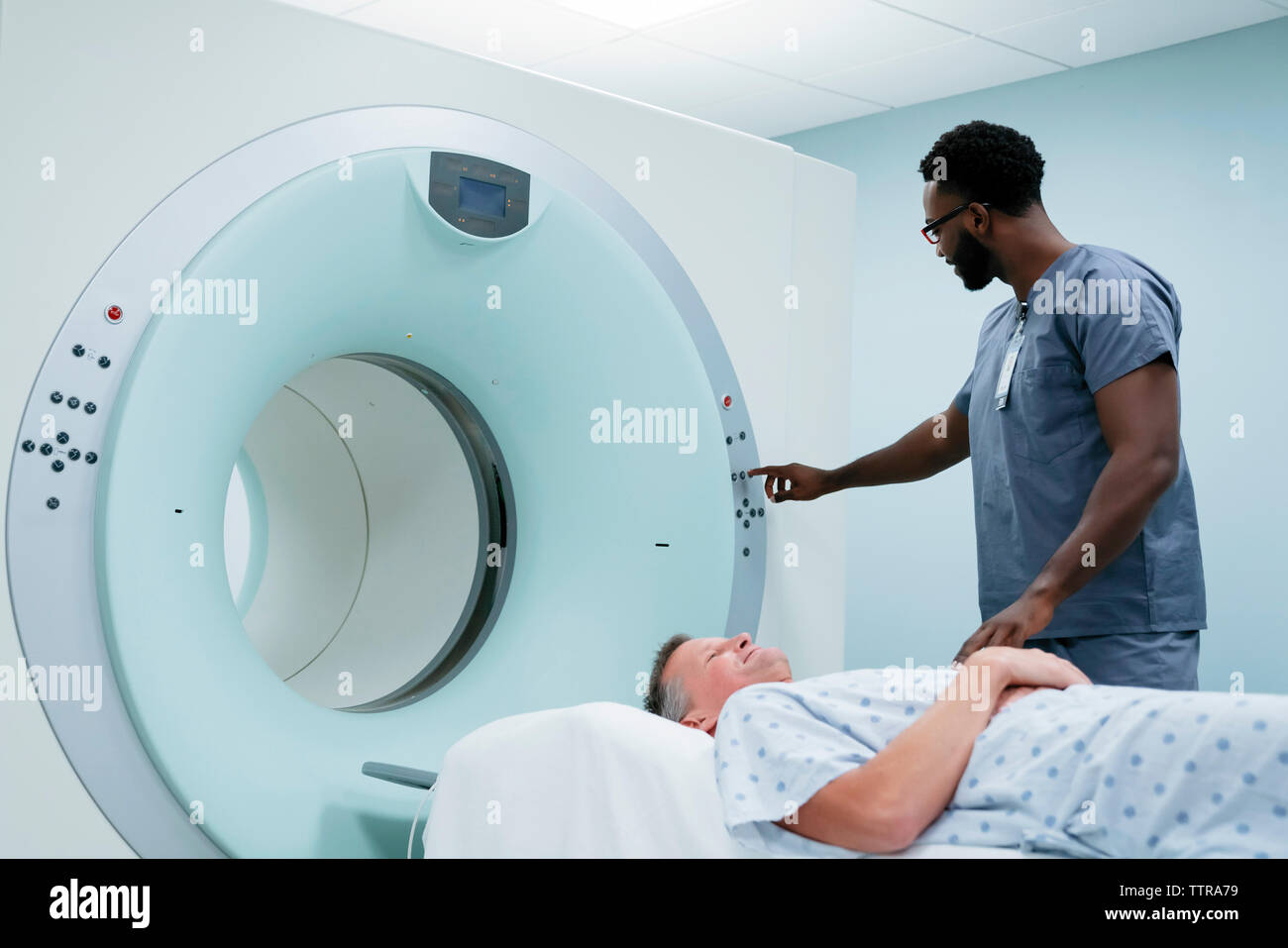 Male nurse adjusting button on MRI Scanner while patient lying in ...