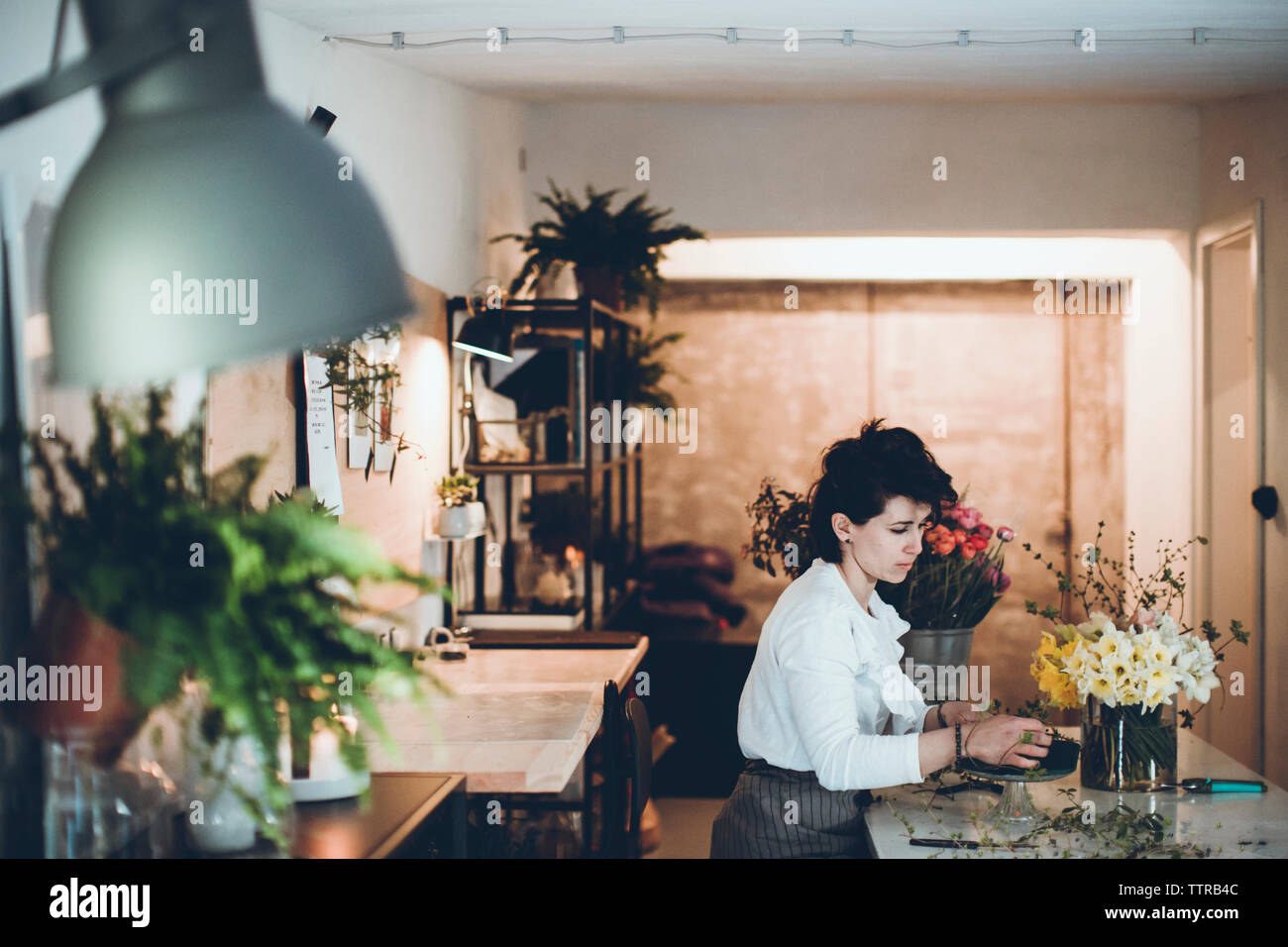 Side view of florist arranging plant stems on floral foams at table in ...