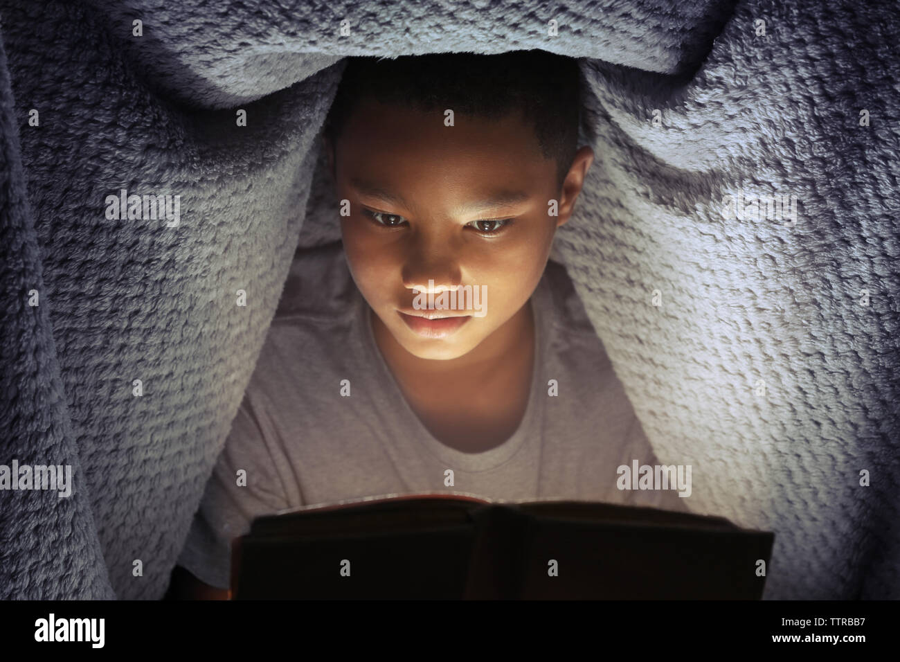 Cute boy reading book at night Stock Photo - Alamy