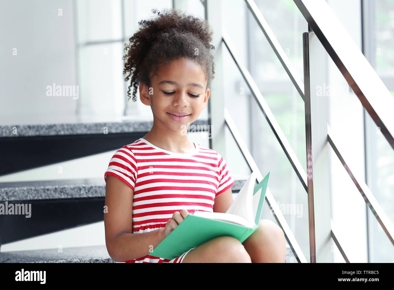 Cute girl reading book on light background Stock Photo - Alamy