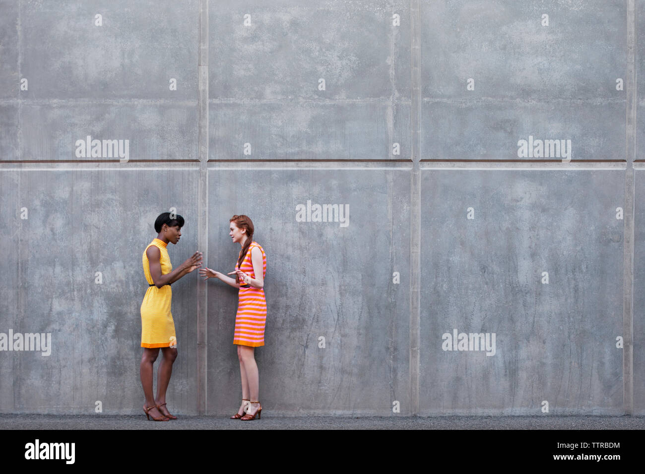 Full length of multi-ethnic friends talking while standing against wall ...