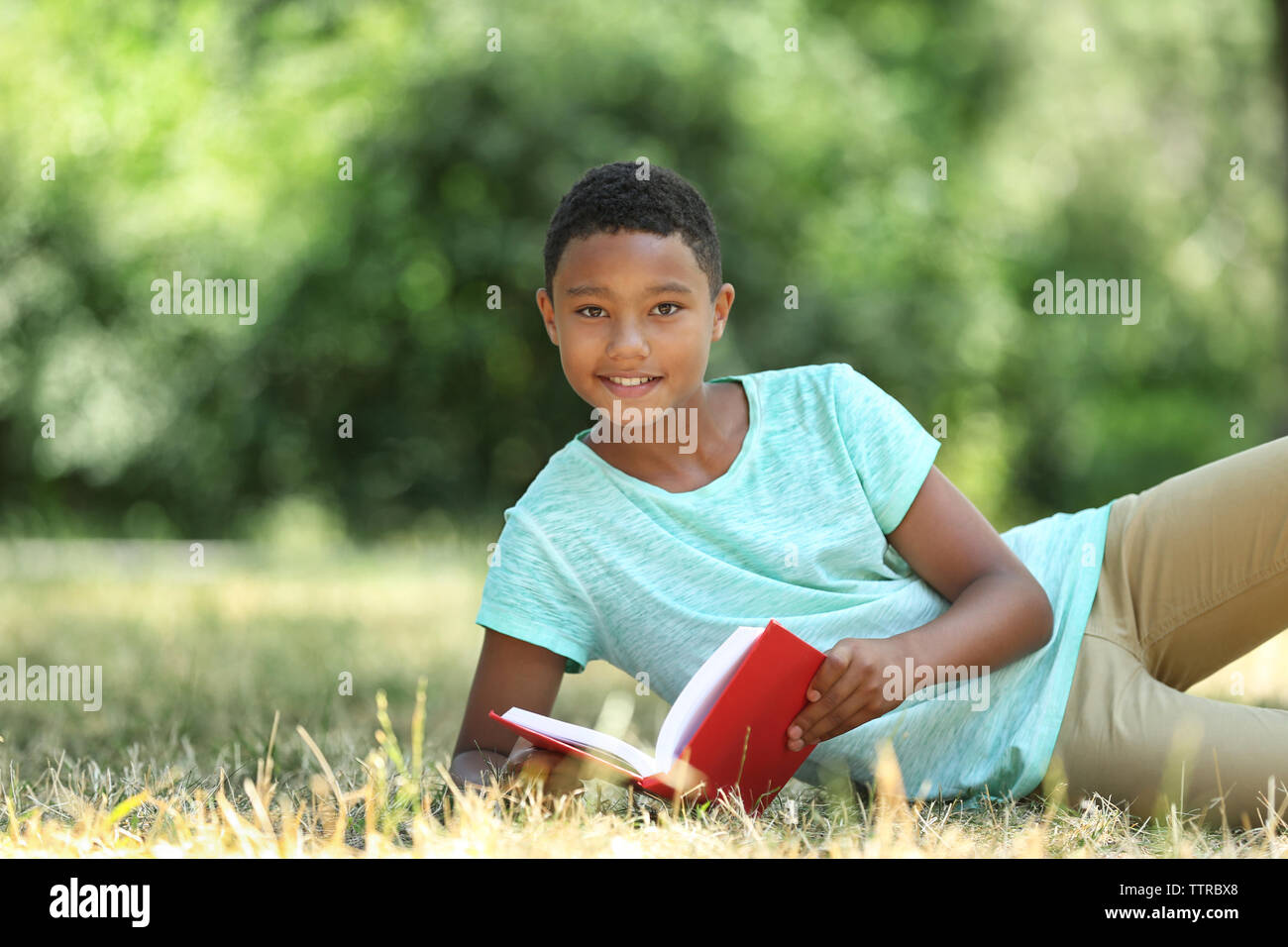 Cute boy reading book on green grass Stock Photo - Alamy
