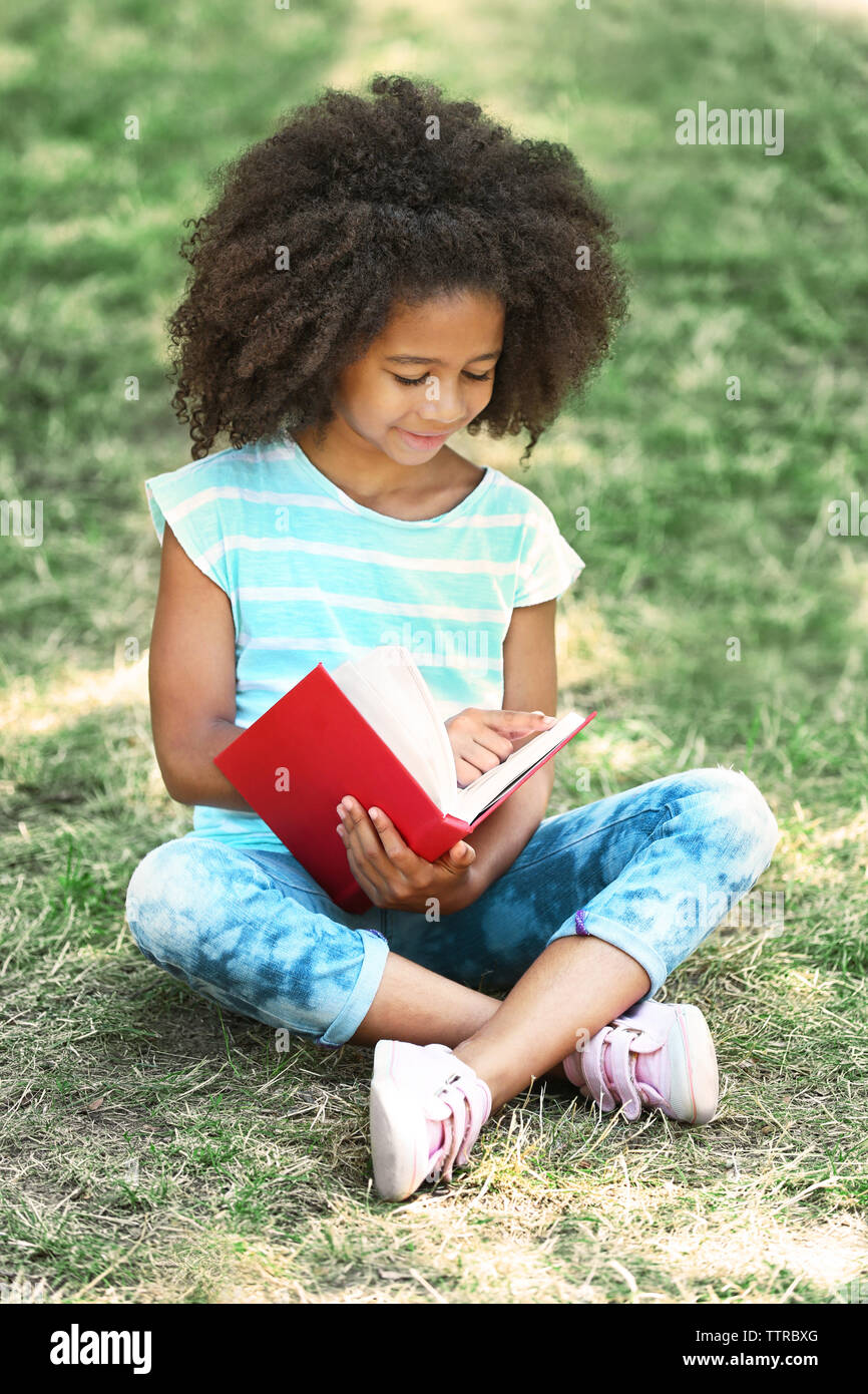 Cute girl reading book on green grass Stock Photo - Alamy