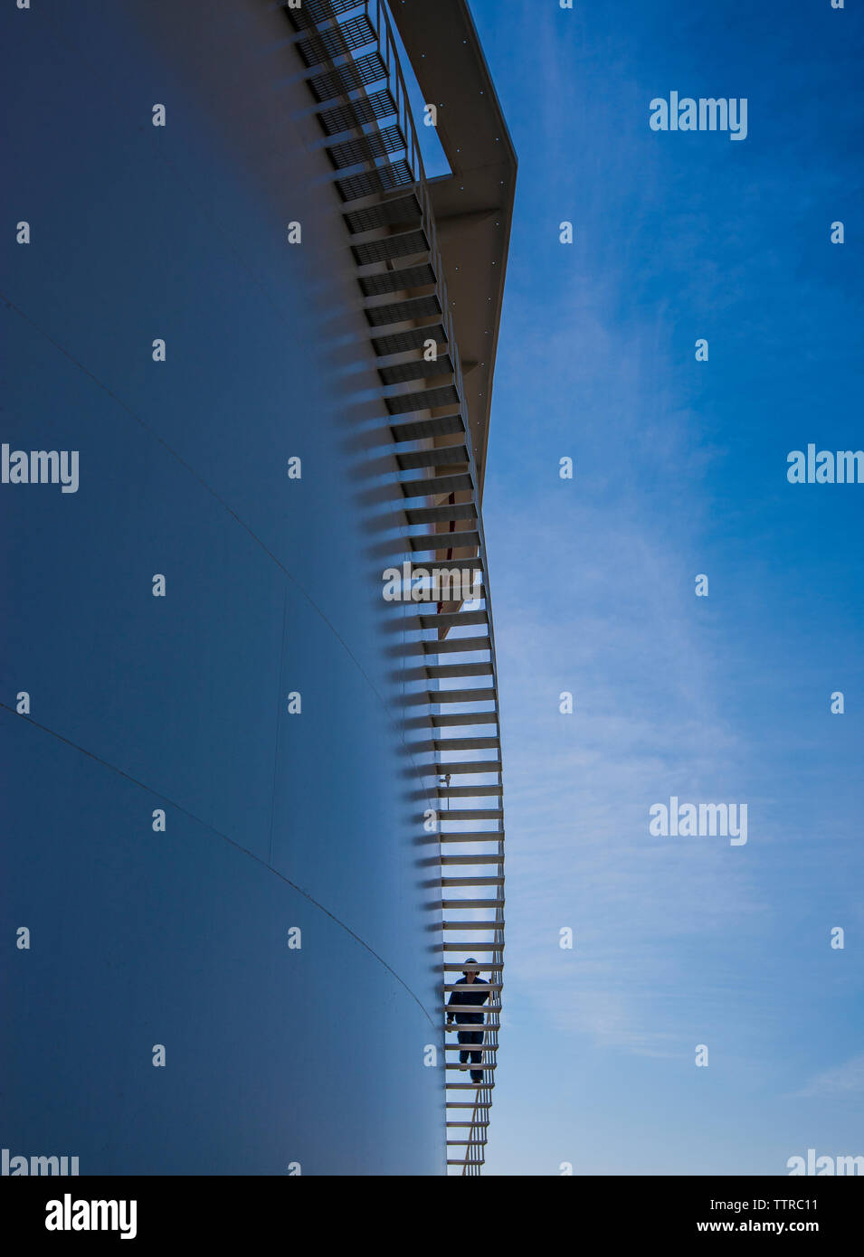 Low angle view of worker moving up steps of storage tank at oil ...