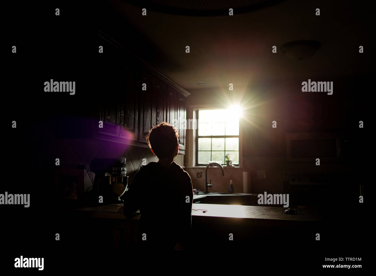 Silhouette boy looking bright sun through window while standing in ...
