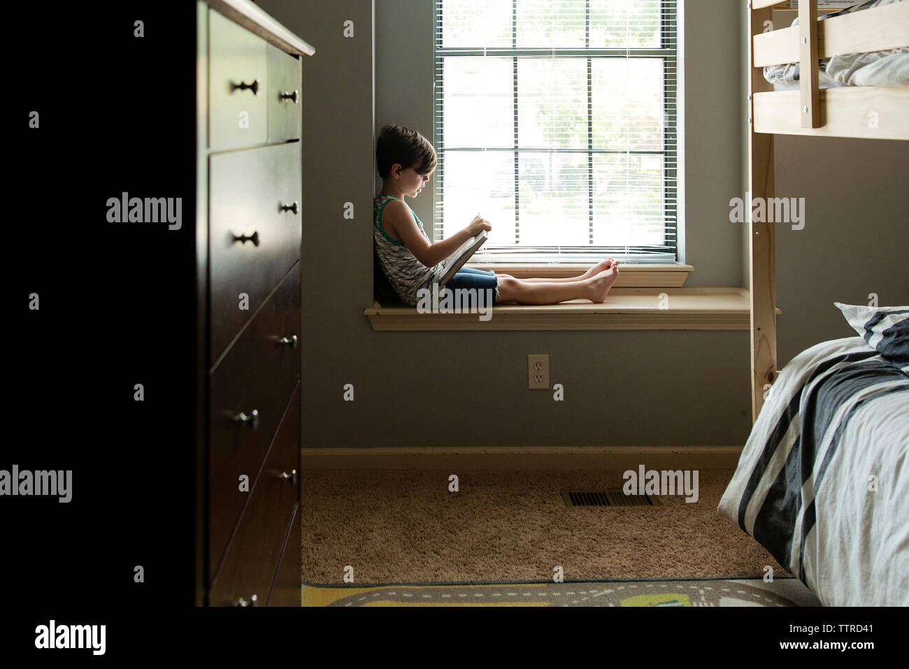 Boy reading book while sitting on window sill Stock Photo - Alamy
