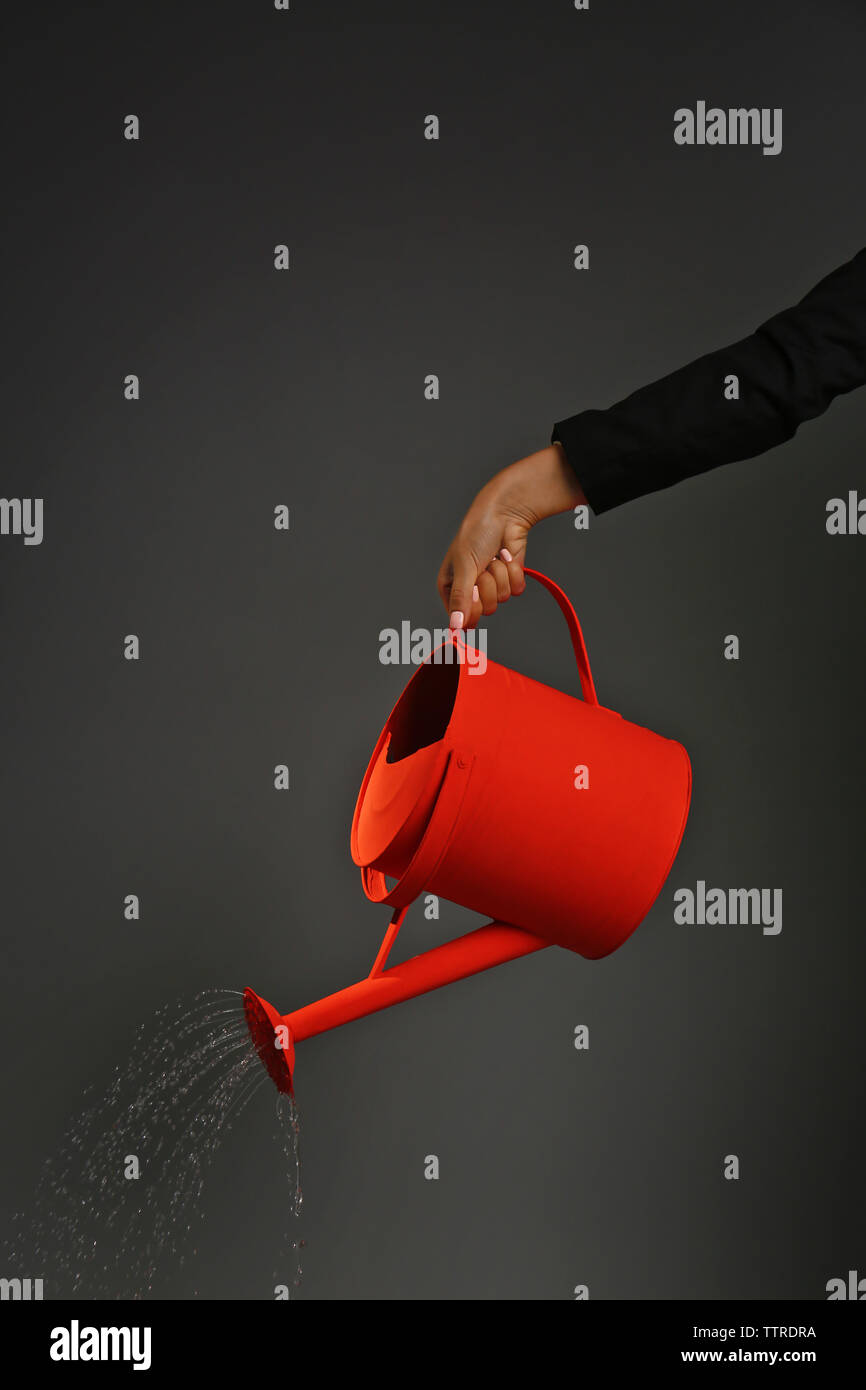 Hand holding watering can on dark grey background Stock Photo - Alamy