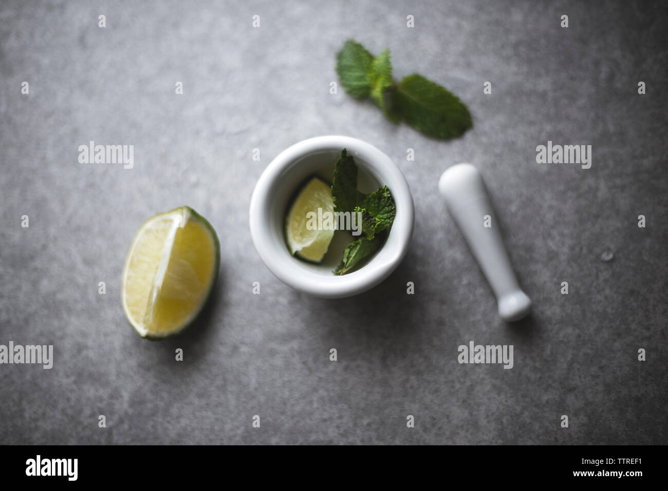 Overhead view of lemon and mint leaves in mortar by pestle on kitchen ...