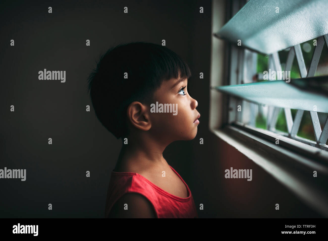 Side view of boy looking through window while standing at home Stock ...