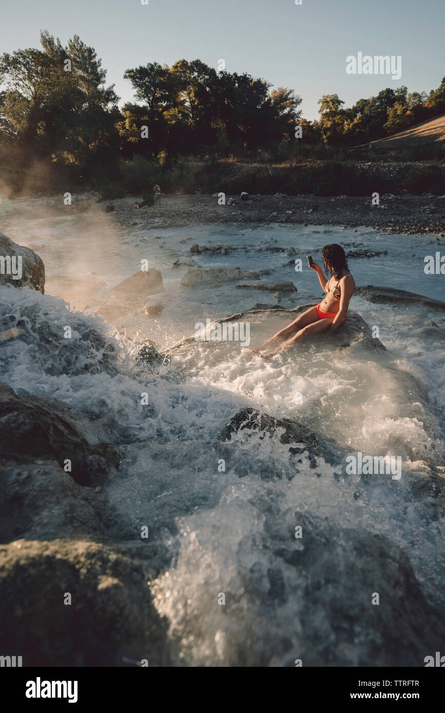 High angle view of woman sitting on rocks while enjoying in steam ...