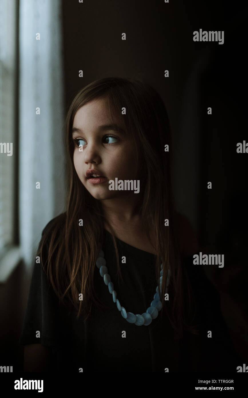 Close-up of thoughtful girl looking through window while standing in ...