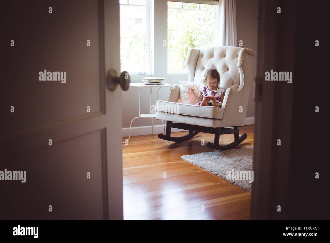 Girl reading picture book while sitting on rocking chair at home seen ...