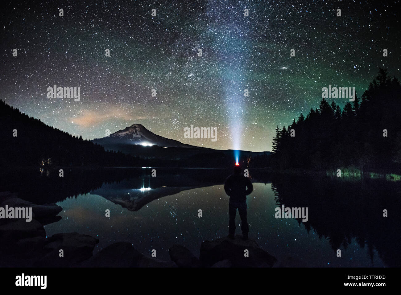 Silhouette man wearing headlamp standing at lakeshore against starry ...