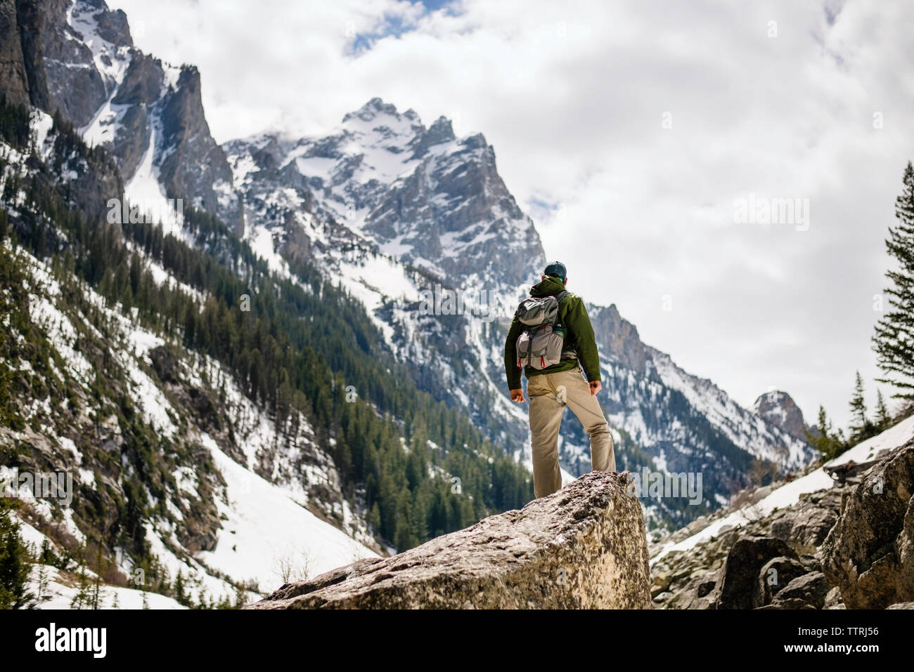 Rear view of hiker standing on rock against snowcapped mountain Stock ...