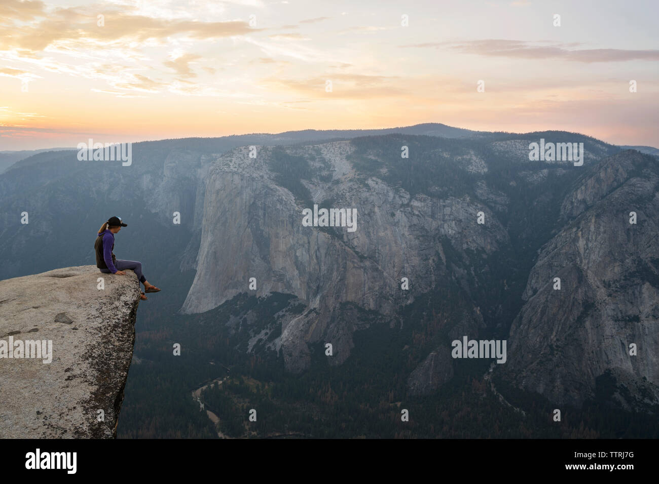 Side view of woman sitting on cliff during sunset Stock Photo - Alamy