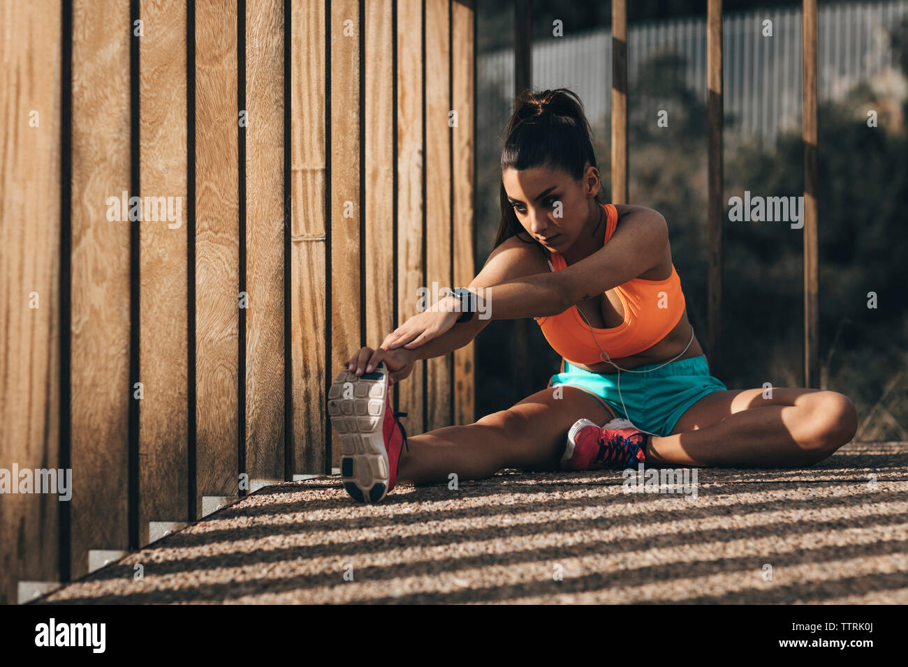 Female athlete exercising while sitting by wooden railing Stock Photo ...