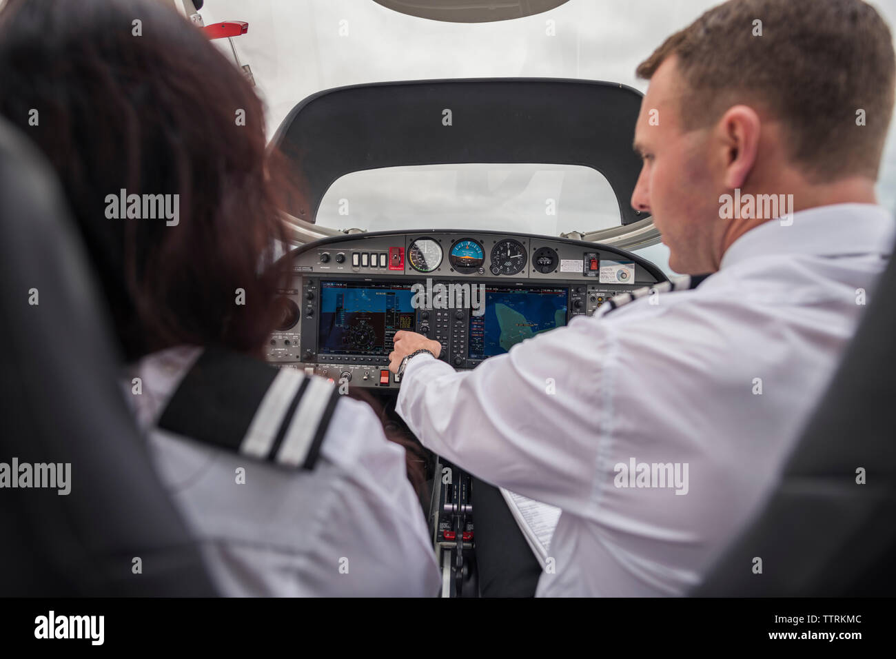 Rear view of male pilot explaining dashboard to female trainee while ...