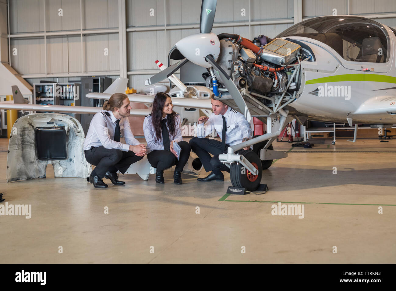 Engineer showing airplane wheel to trainees while crouching on floor in ...
