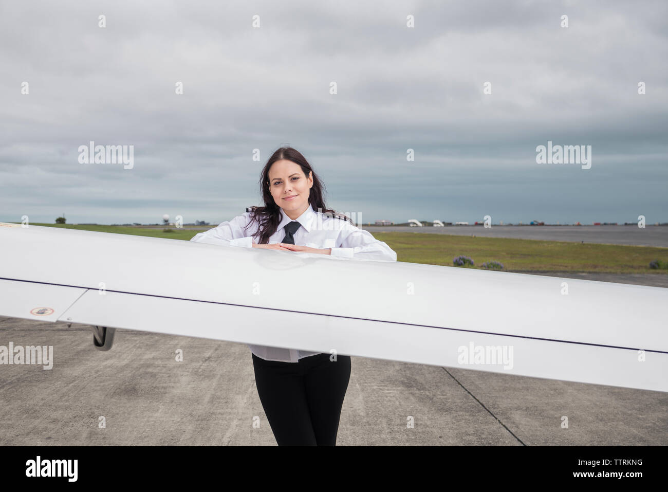 Portrait of confident female pilot standing by aircraft wing against ...