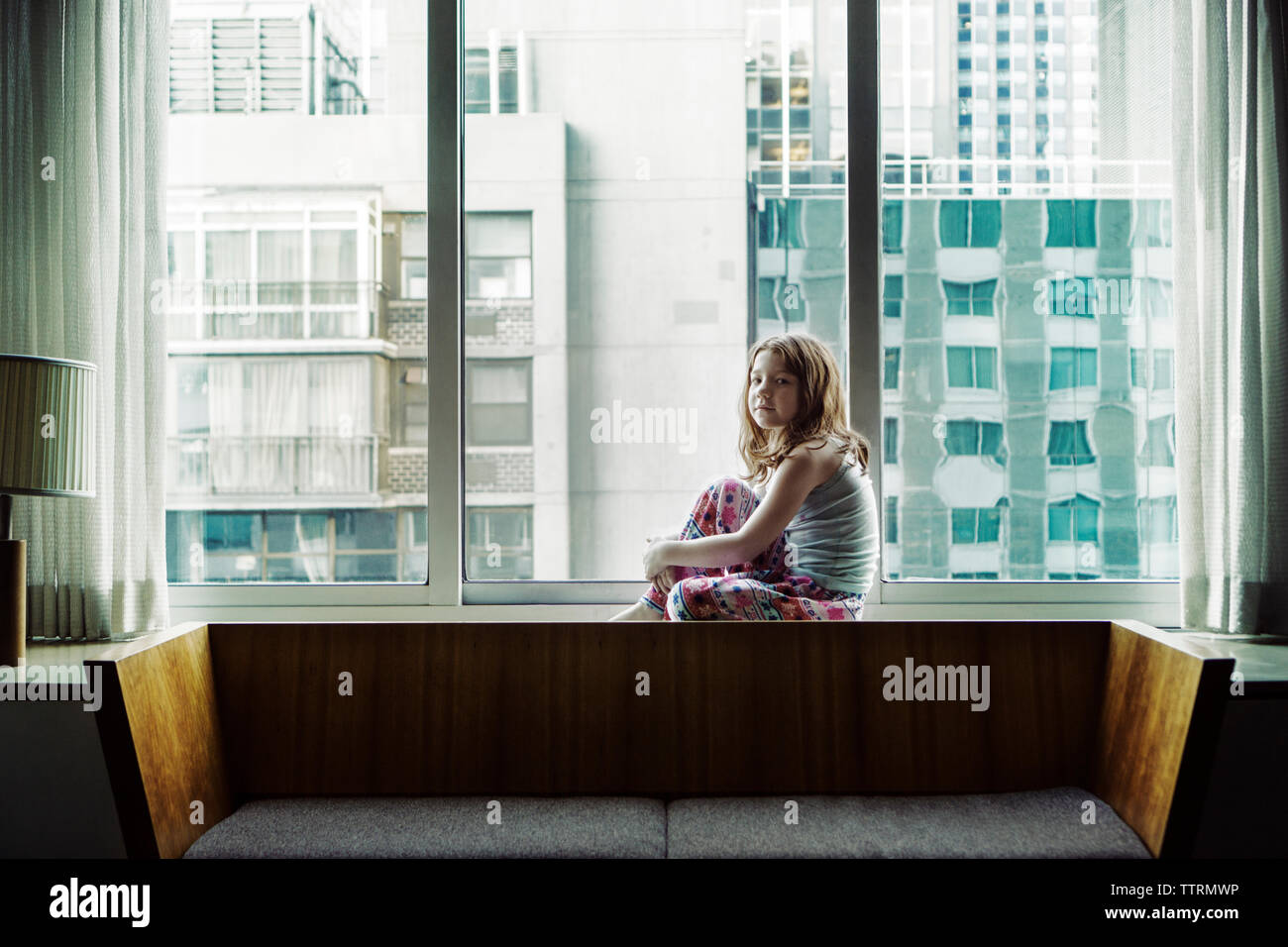 Portrait of girl sitting against window at home Stock Photo - Alamy