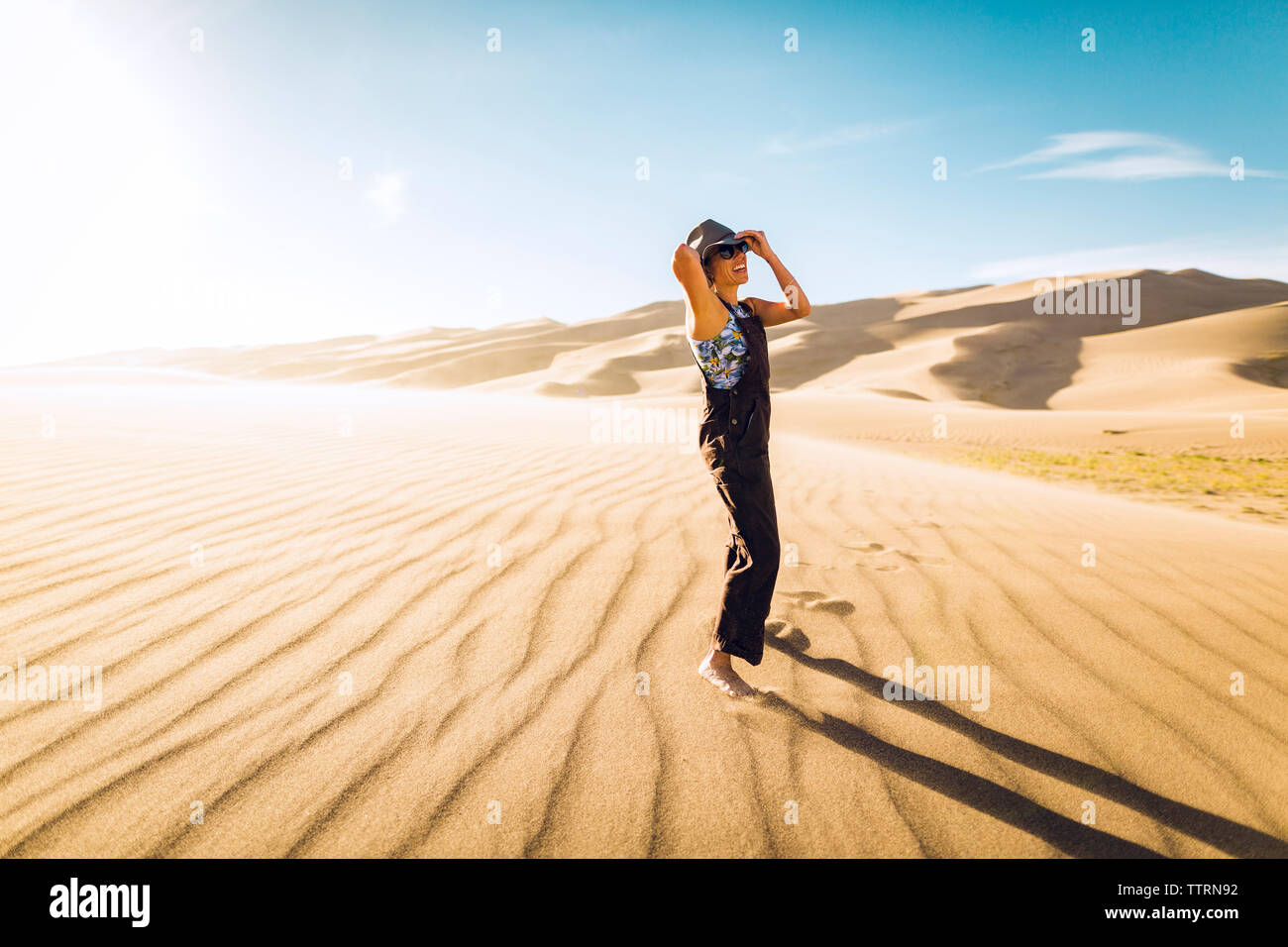 Side view of woman adjusting hat while standing at Great Sand Dunes ...